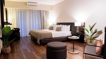 Quarto de hotel moderno com uma cama grande, uma mesa de cabeceira, uma pequena mesa redonda e um espaço de estar com uma poltrona.