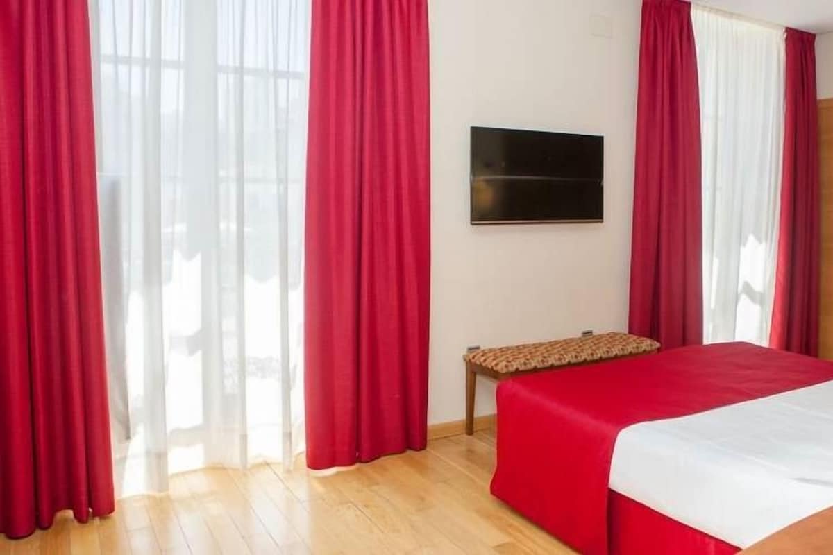 Quarto de hotel com cama, televisão e guarda-roupa de madeira.