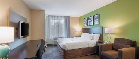 Quarto de hotel com cama, escrivaninha, cadeira, televisão e janela com cortinas.