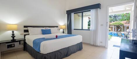 Quarto de hotel com uma cama, duas mesas de cabeceira com luminárias, vista para uma piscina e um ventilador de teto.
