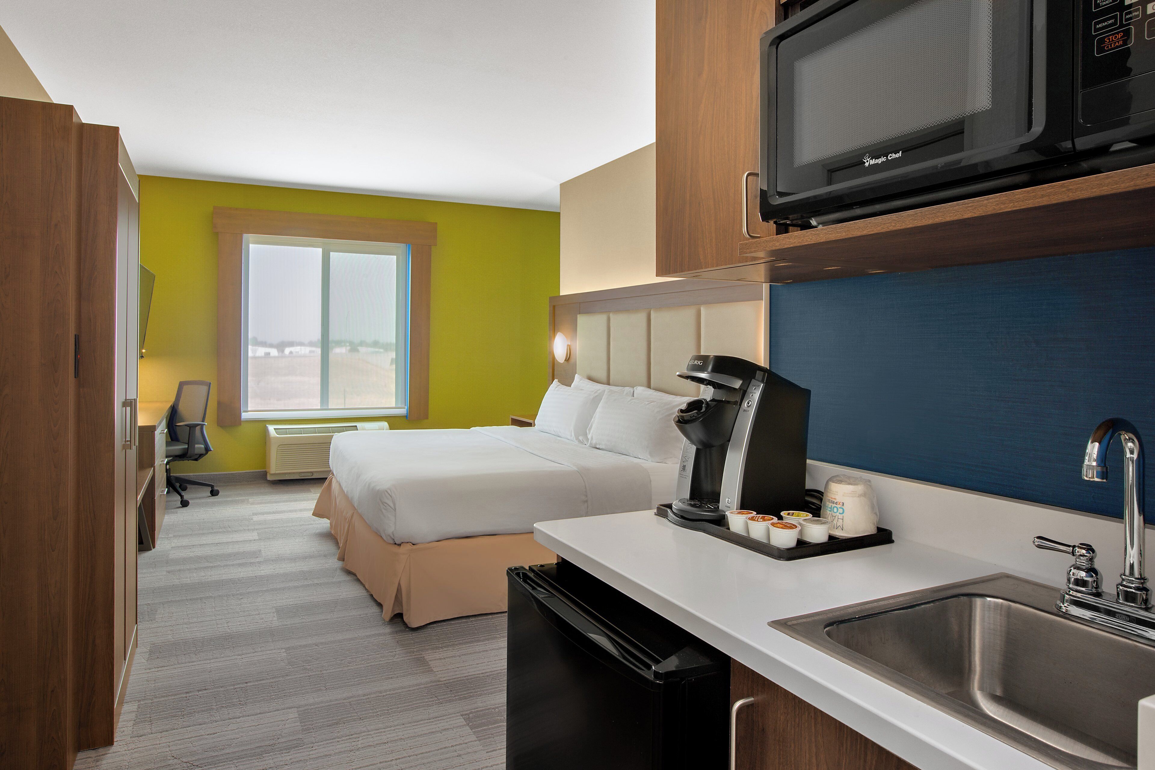 Quarto de hotel com cama, máquina de café, pia e micro-ondas.