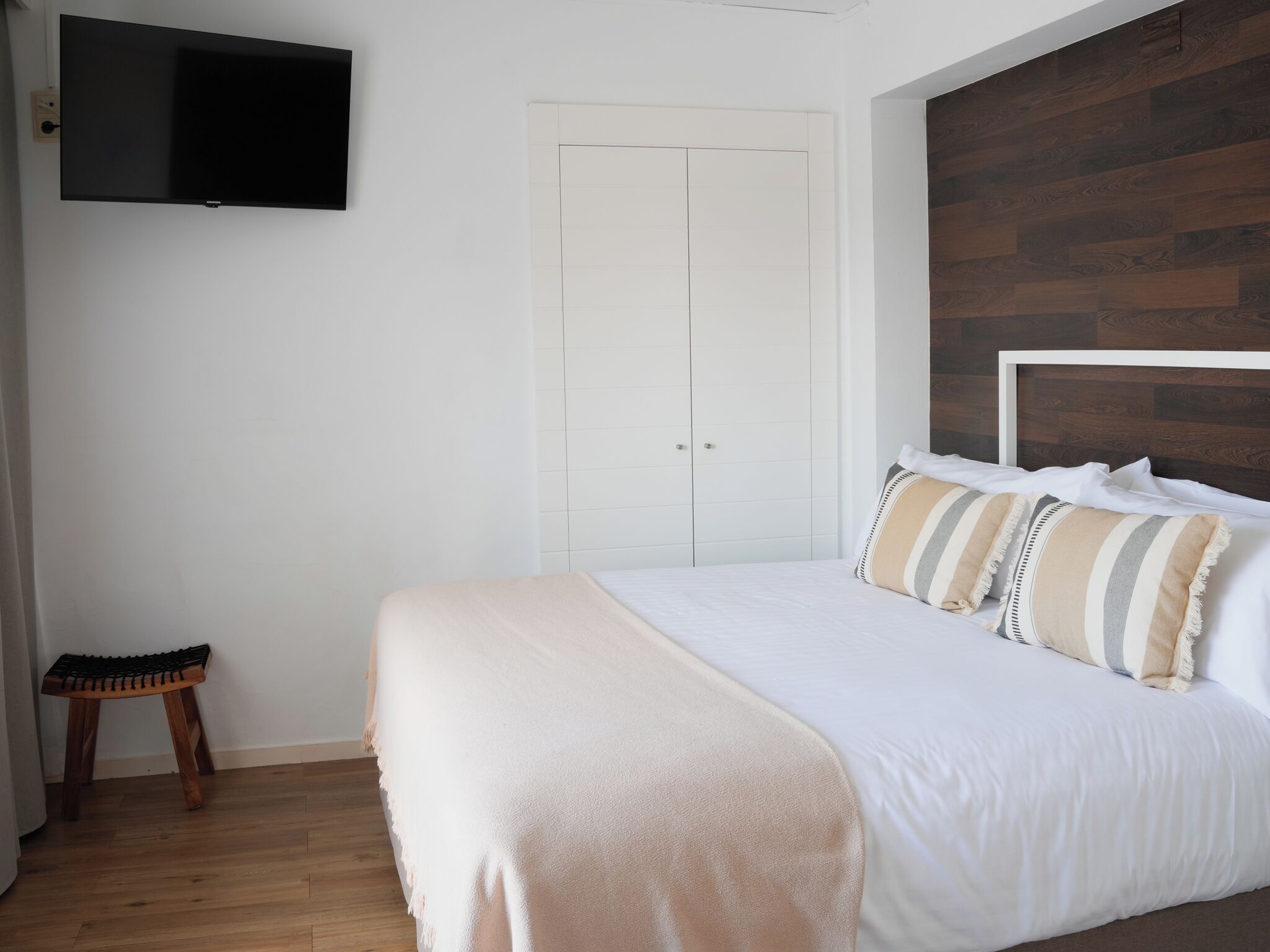 Quarto com cama, televisão na parede, piso de madeira e porta branca.
