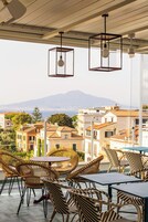 Um terraço com mobiliário de vime e luminárias pendentes, com vista para um horizonte urbano com edifícios e uma montanha.