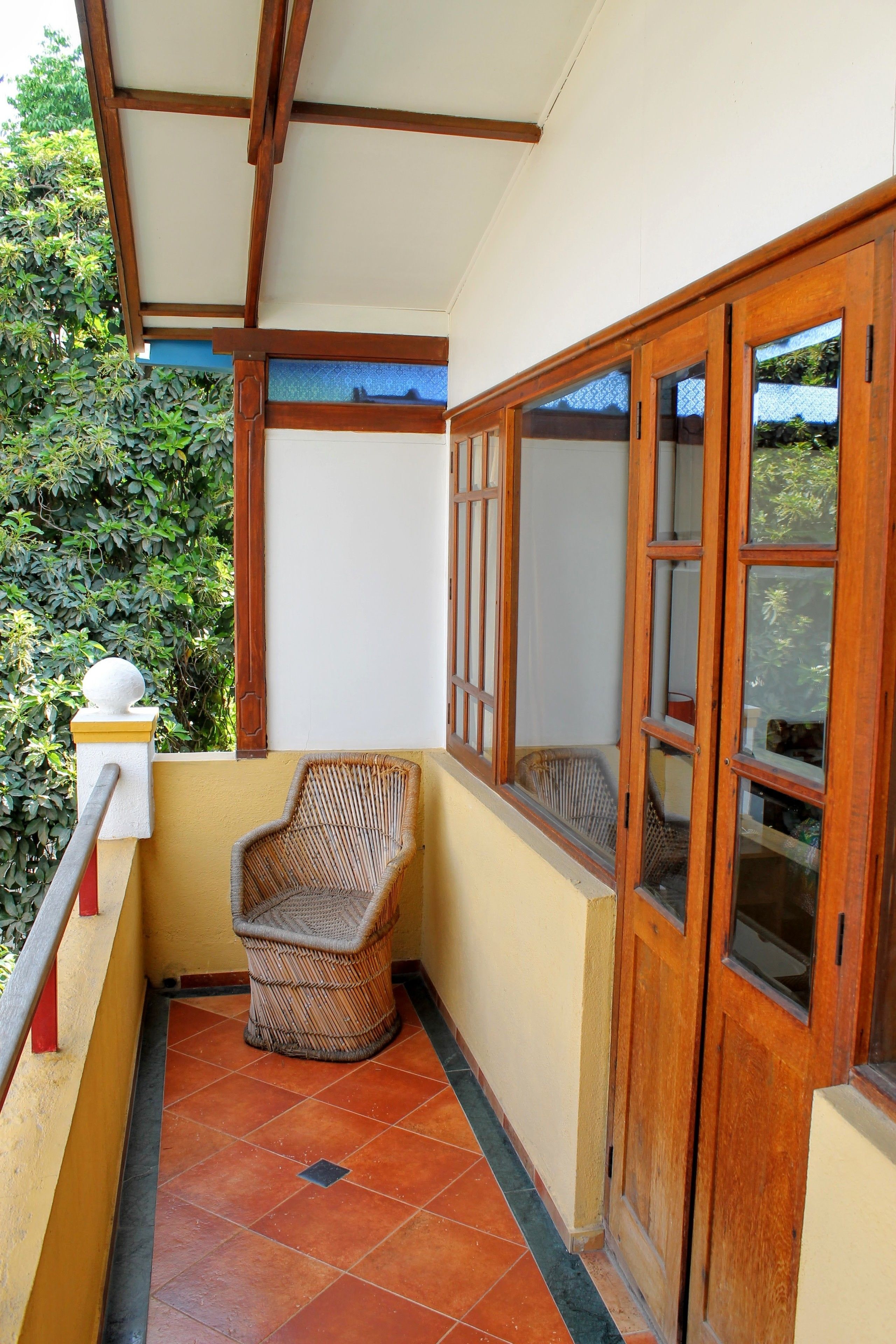 Uma varanda com cadeira de vime, porta de madeira e chão de azulejos.