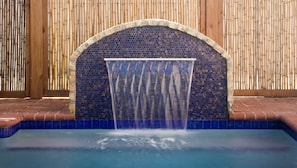 Piscina com parede de mosaico azul e arco de pedra.