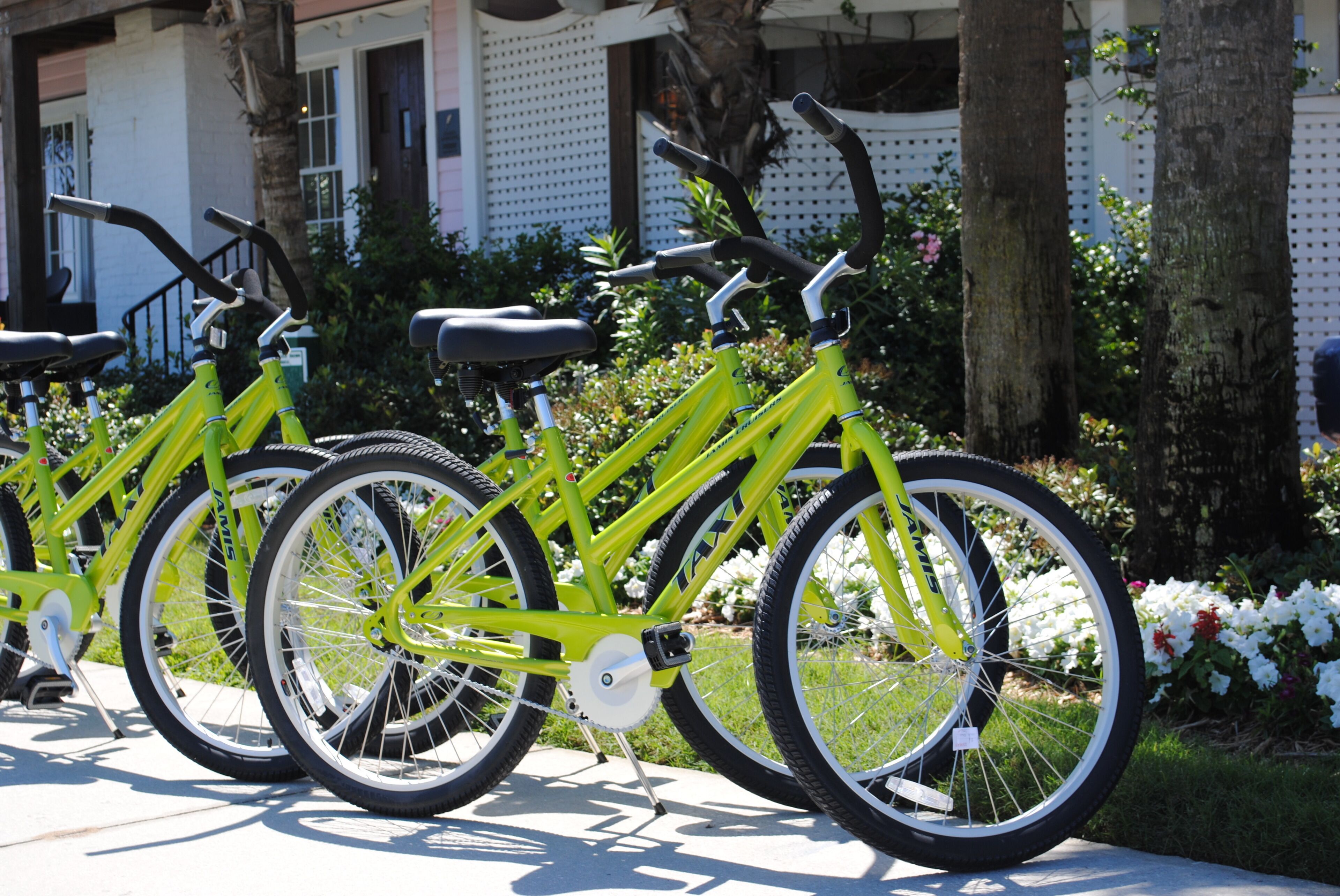 Uma fileira de bicicletas amarelas estacionadas em frente a um edifício com cerca branca e vegetação.
