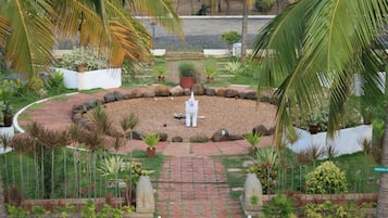 Um jardim circular com uma estátua branca no centro, rodeado por palmeiras e diversas plantas.