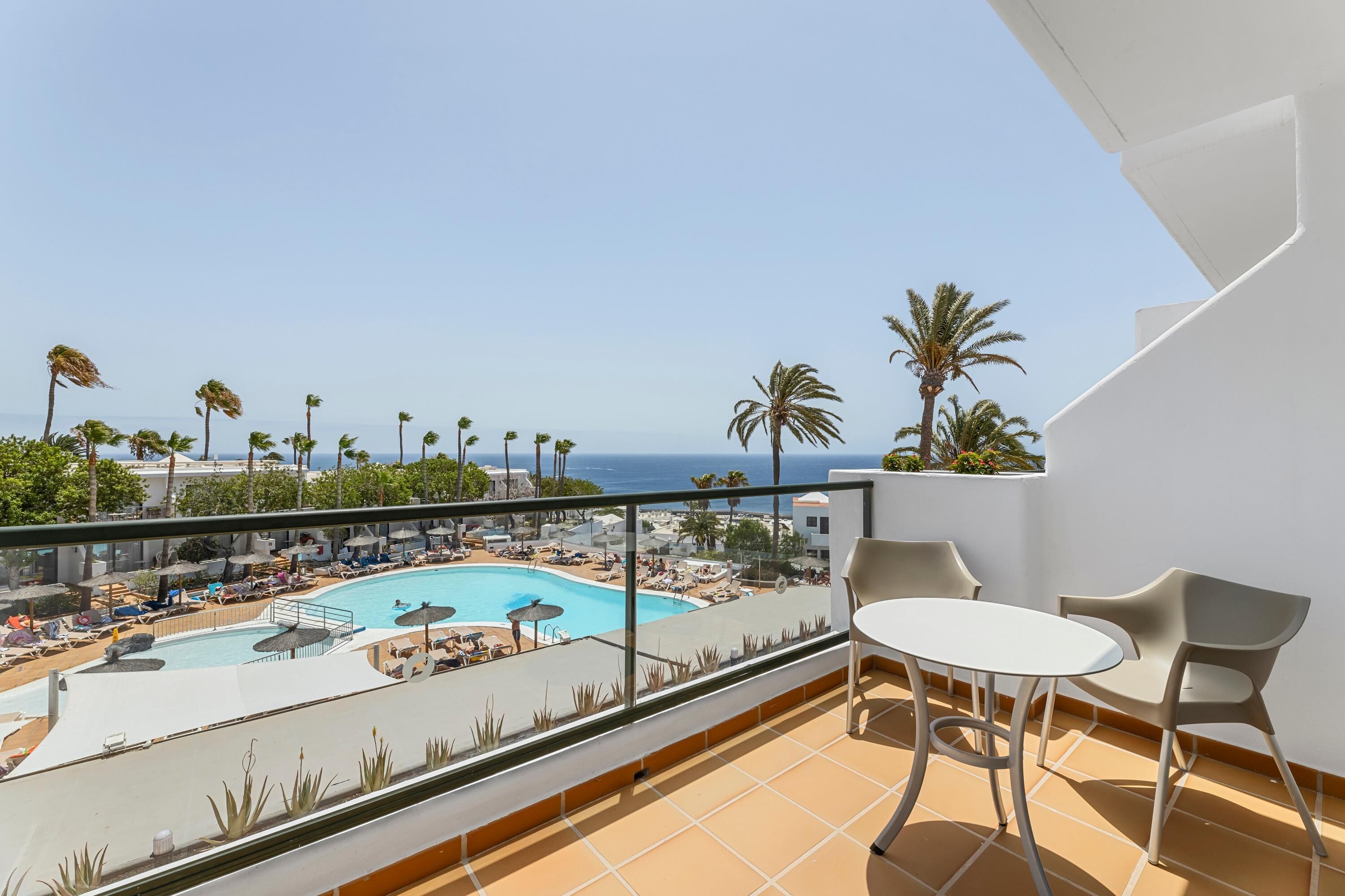 Varanda com vista para piscina e praia, incluindo cadeiras de sol e guarda-sóis.
