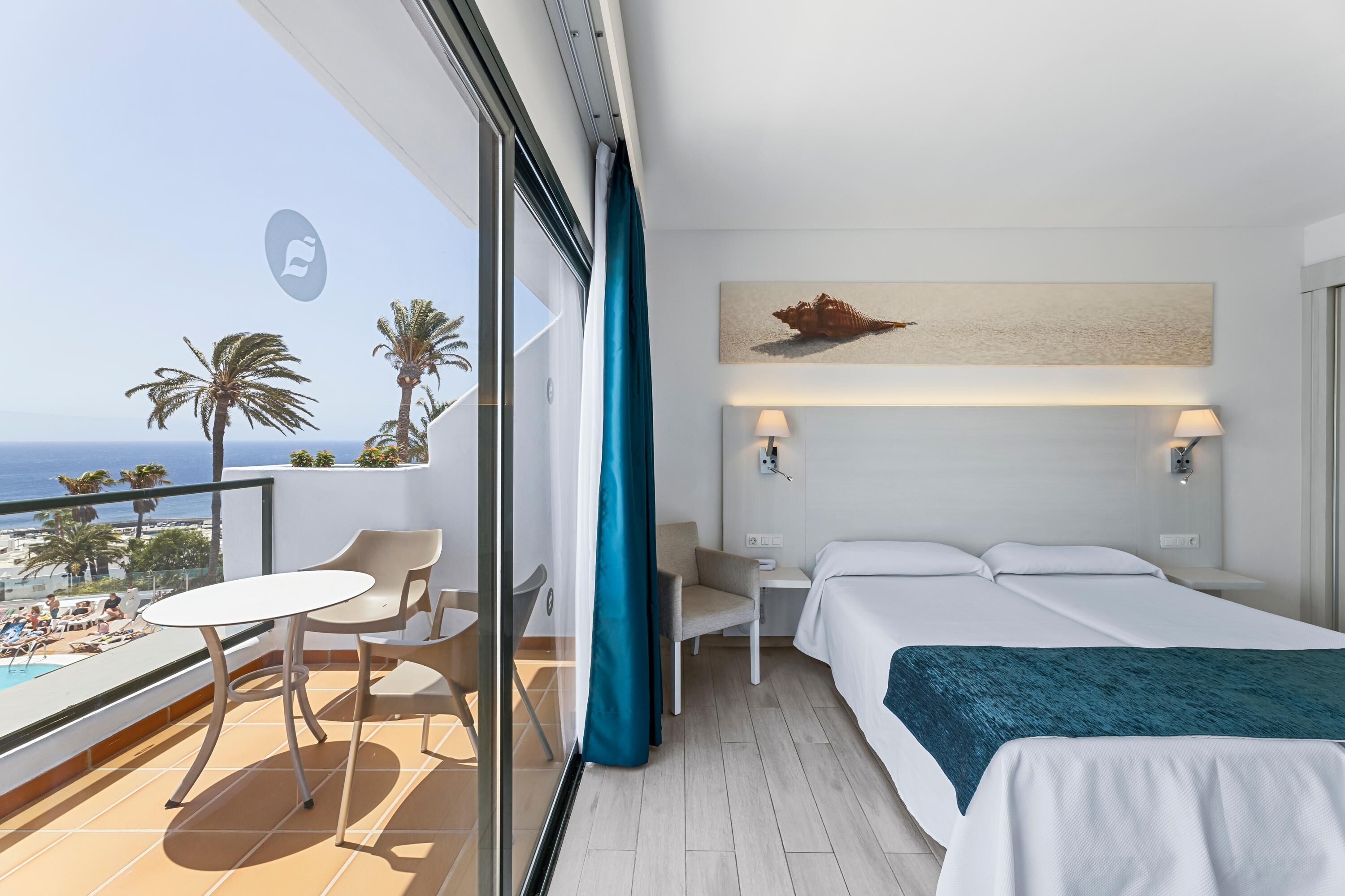 Quarto de hotel com varanda, cama, escrivaninha e cadeira.