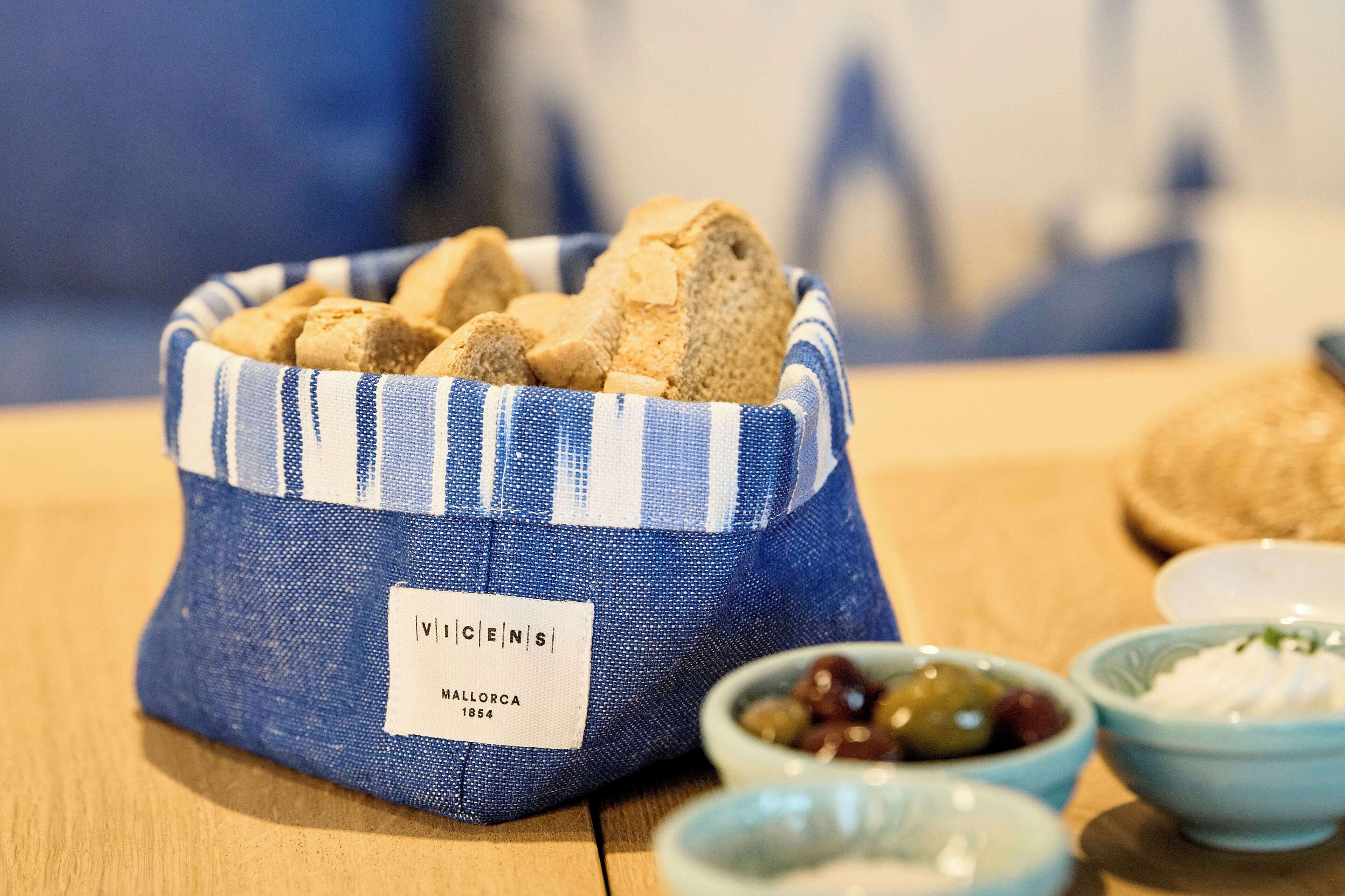 Uma cesta de pão com a etiqueta 'VICENS' num recipiente azul e branco listrado.