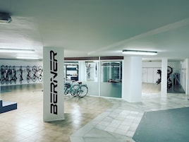 Um espaço amplo e interno com piso ladrilhado, um grande pilar com a palavra "BERNER" e várias bicicletas fixadas na parede.