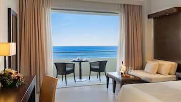 Quarto de hotel com cama, escrivaninha, cadeira, mesinha e vista para o oceano.