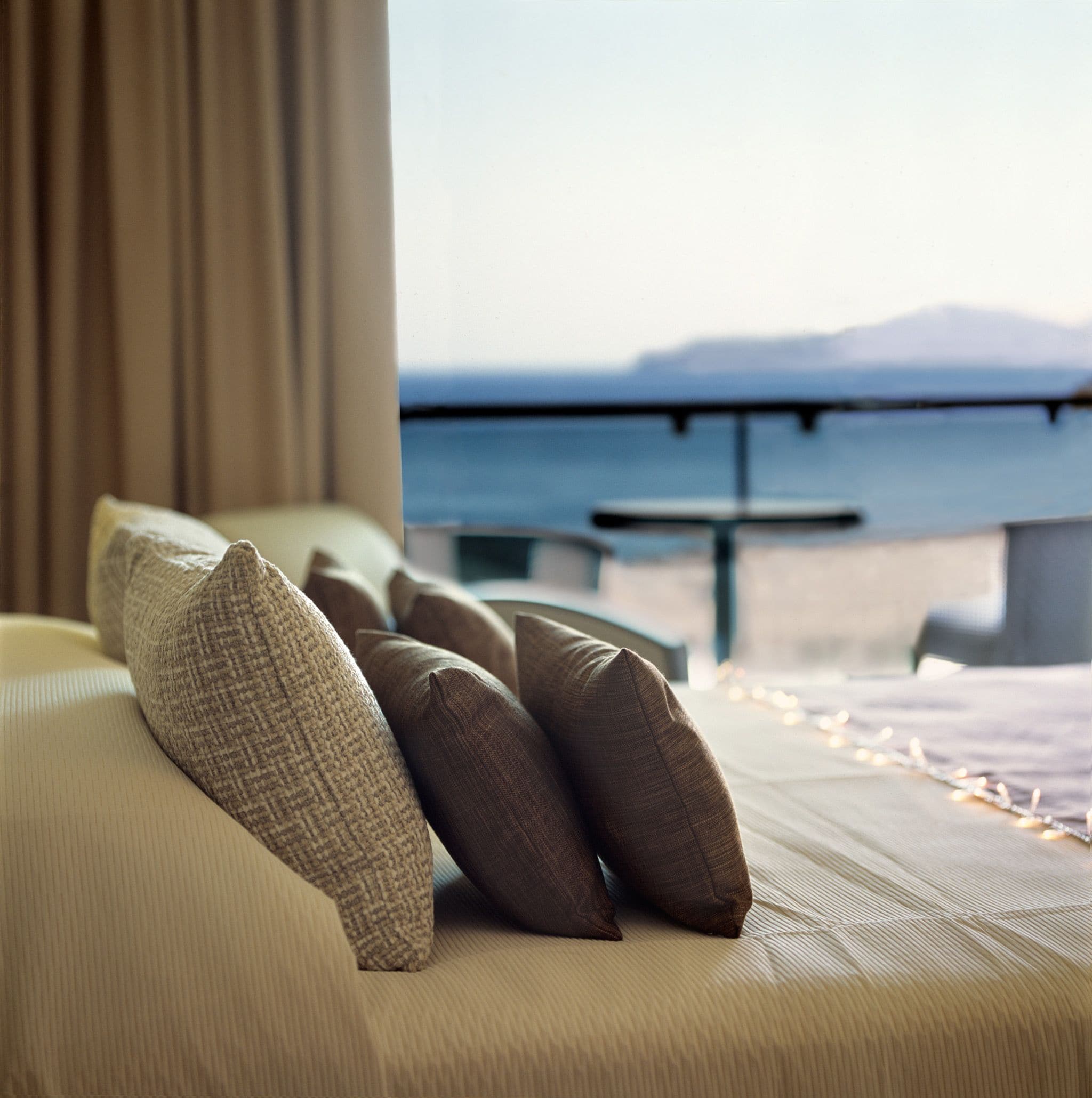 Quarto de hotel com cama, almofadas e vista para o mar.