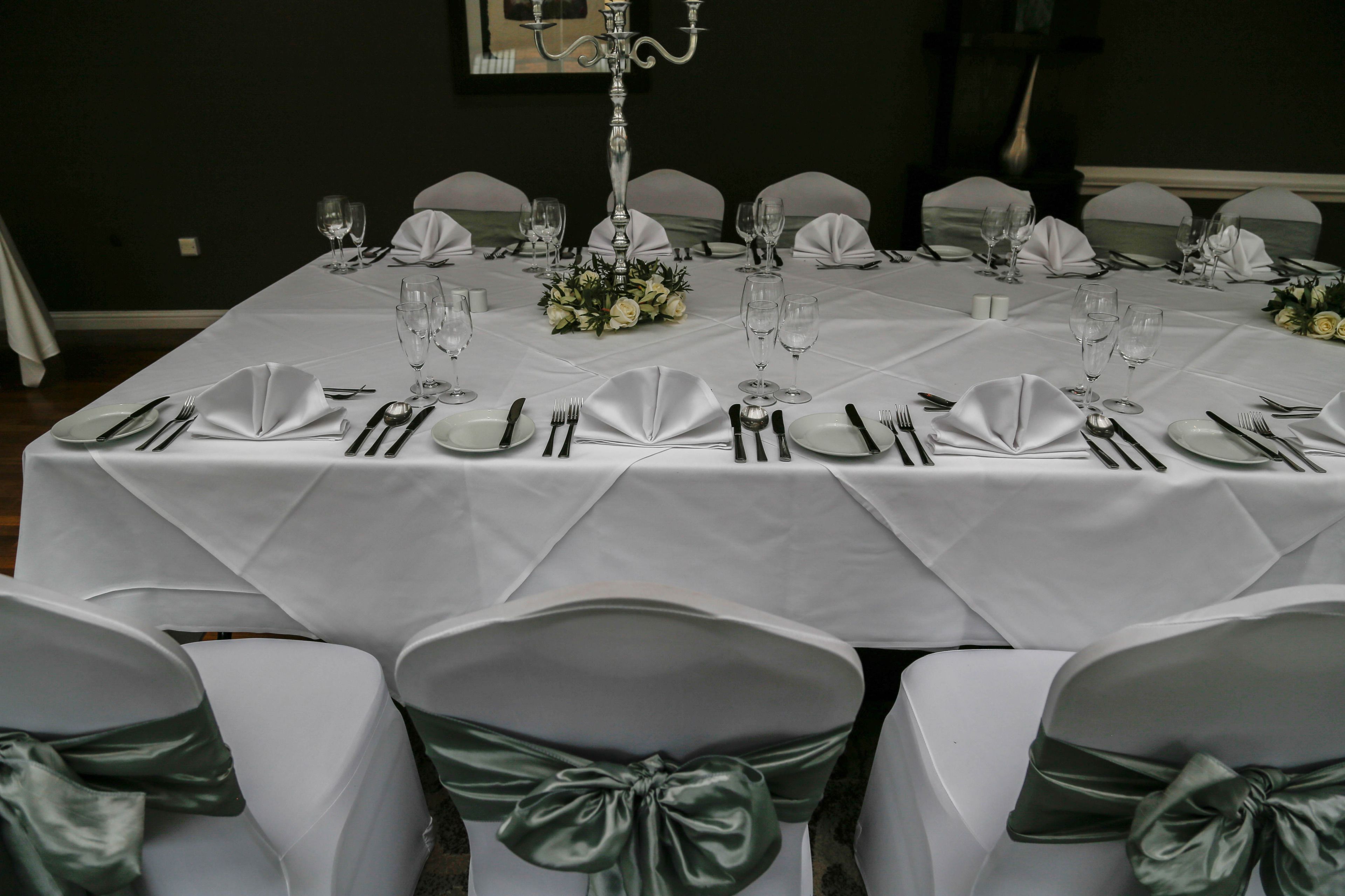 Uma mesa de banquete posta para um evento formal, com toalhas brancas, talheres e taças.