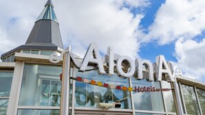 Um hotel com um grande letreiro de 'Aloha', fachada de vidro moderna e um telhado cônico característico.