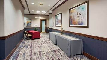 Corredor de hotel com uma mesa vermelha, uma mesa cinza e quadros nas paredes.