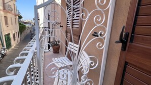 Varanda com grade de metal decorativa, um vaso de planta e uma porta de madeira.