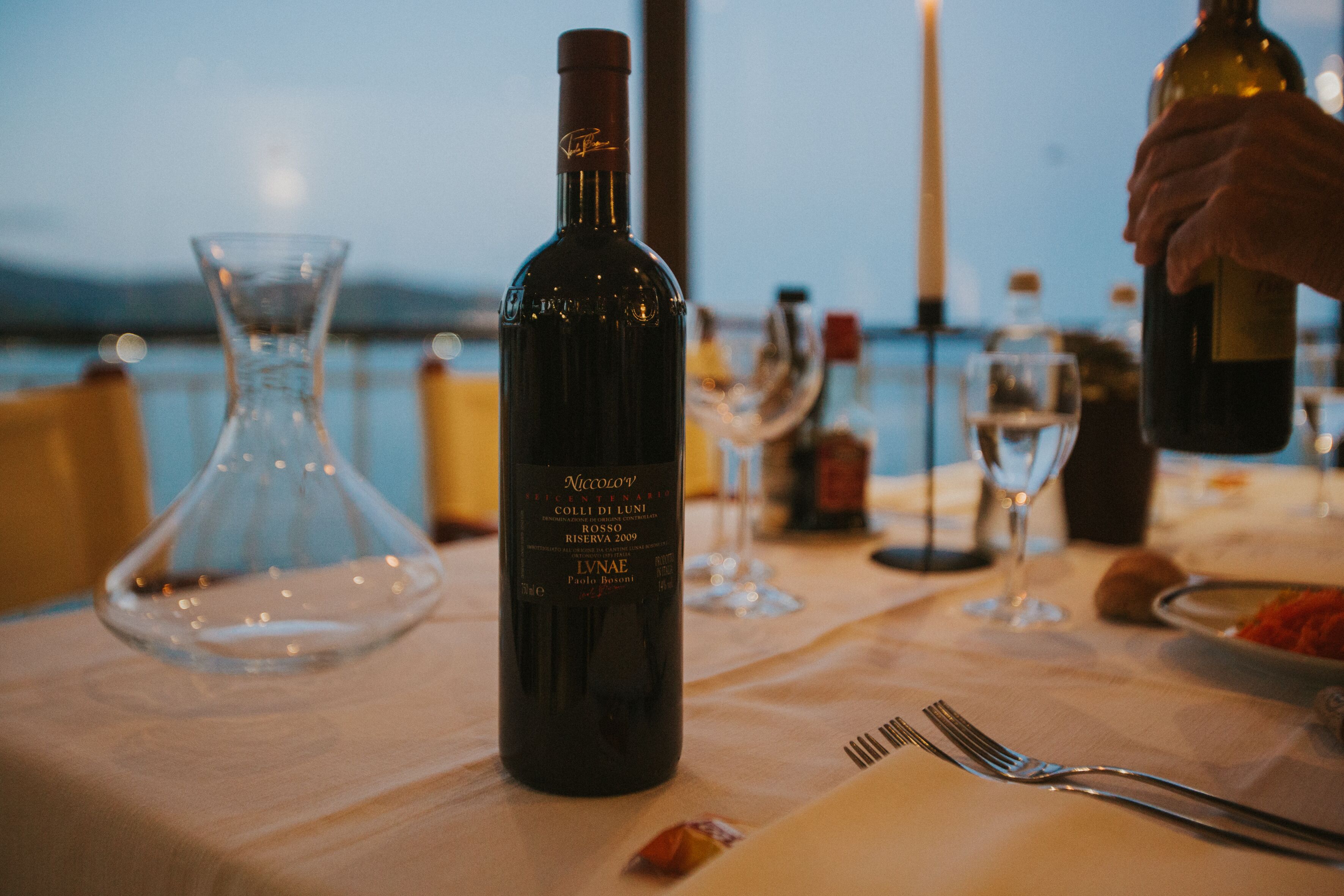 Mesa posta para refeição com garrafa de vinho, copos e uma vela.