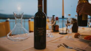 Mesa posta para refeição com garrafa de vinho, copos e uma vela.