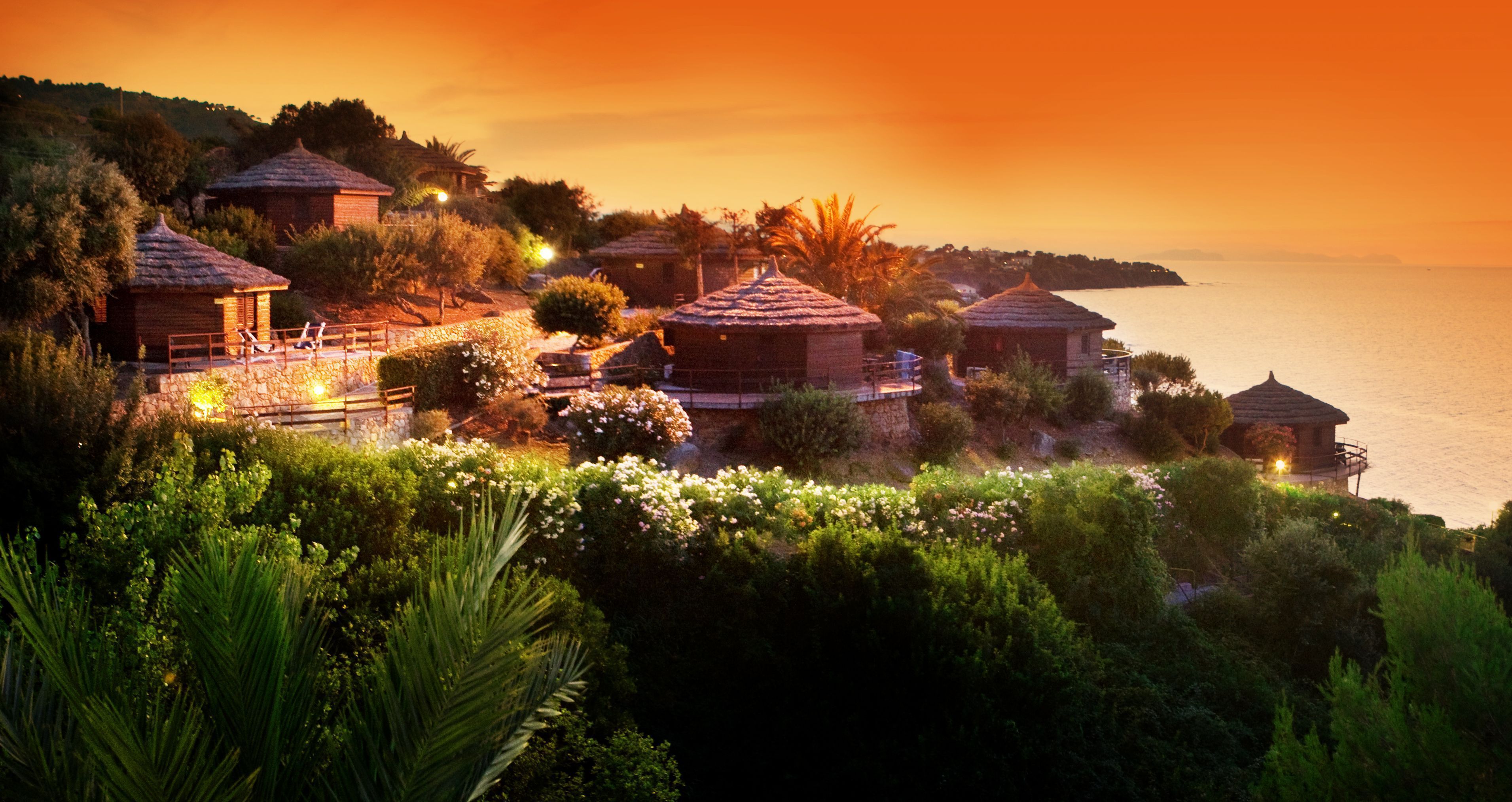 Um resort costeiro com vários edifícios tipo bangalô, vegetação exuberante e vista para o mar.