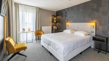 Quarto de hotel moderno com uma cama grande, uma mesinha, uma cadeira e um vaso decorativo.