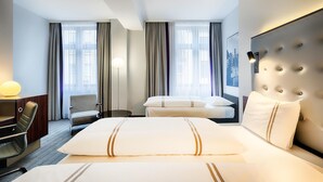 Quarto de hotel com uma cama grande, uma escrivaninha com cadeira, um sofá e cabeceira com luminária.