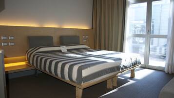 Quarto de hotel moderno com estrutura de cama de madeira, colcha listrada e uma janela grande com cortinas.