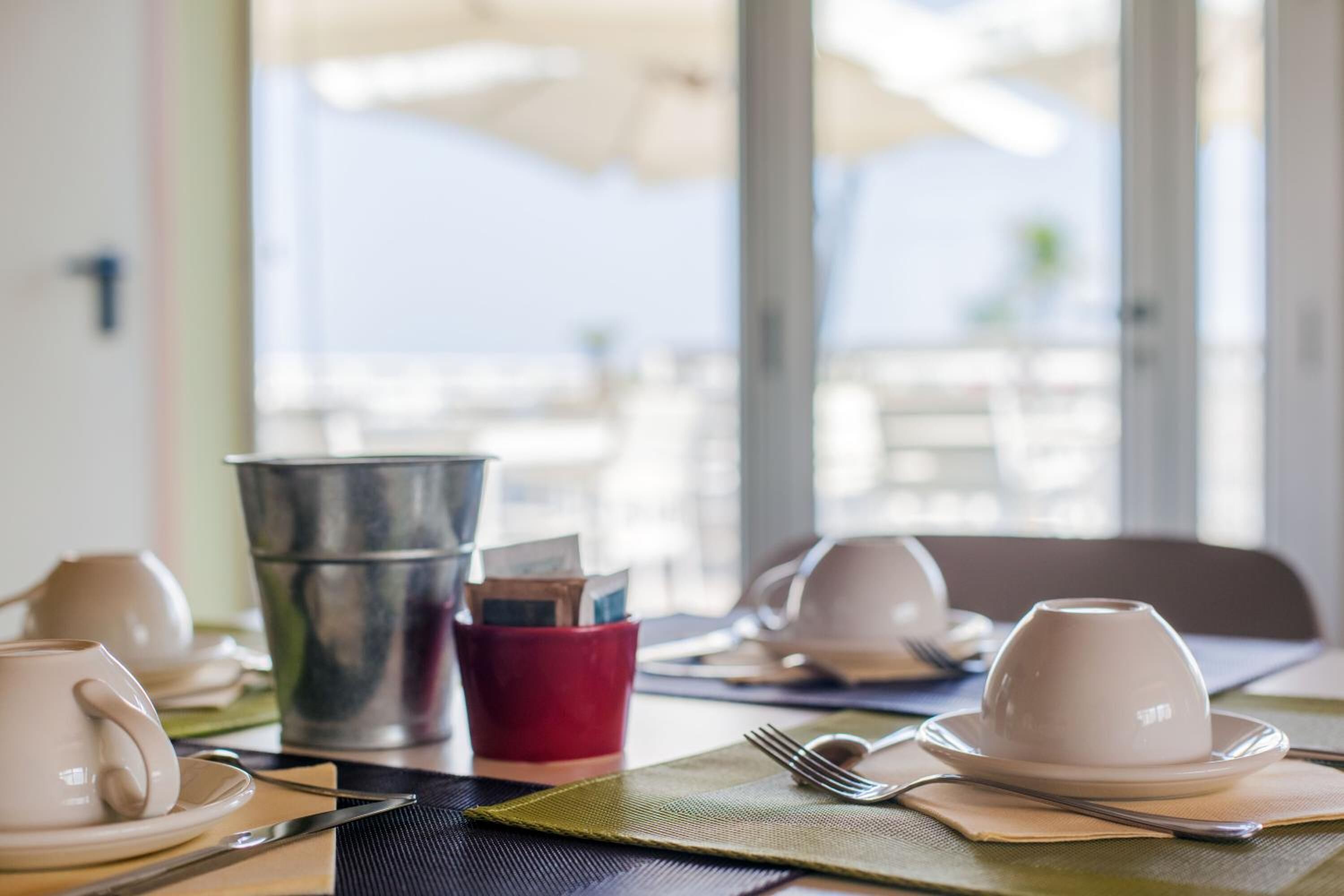 Uma mesa de jantar posta com xícaras, pires brancos e um balde de metal com porta-copos vermelho.