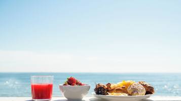 Mesa com um copo de suco vermelho, uma tigela de morangos e um prato de doces com vista para o mar.