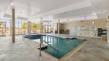 Piscina interna com sinalização clara, cadeira de salva-vidas e área ao redor da piscina com cadeiras e mesas.