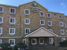 Um hotel de vários andares com fachada de pedra, várias janelas e uma placa com a inscrição "WOODS SPRING SUITES".