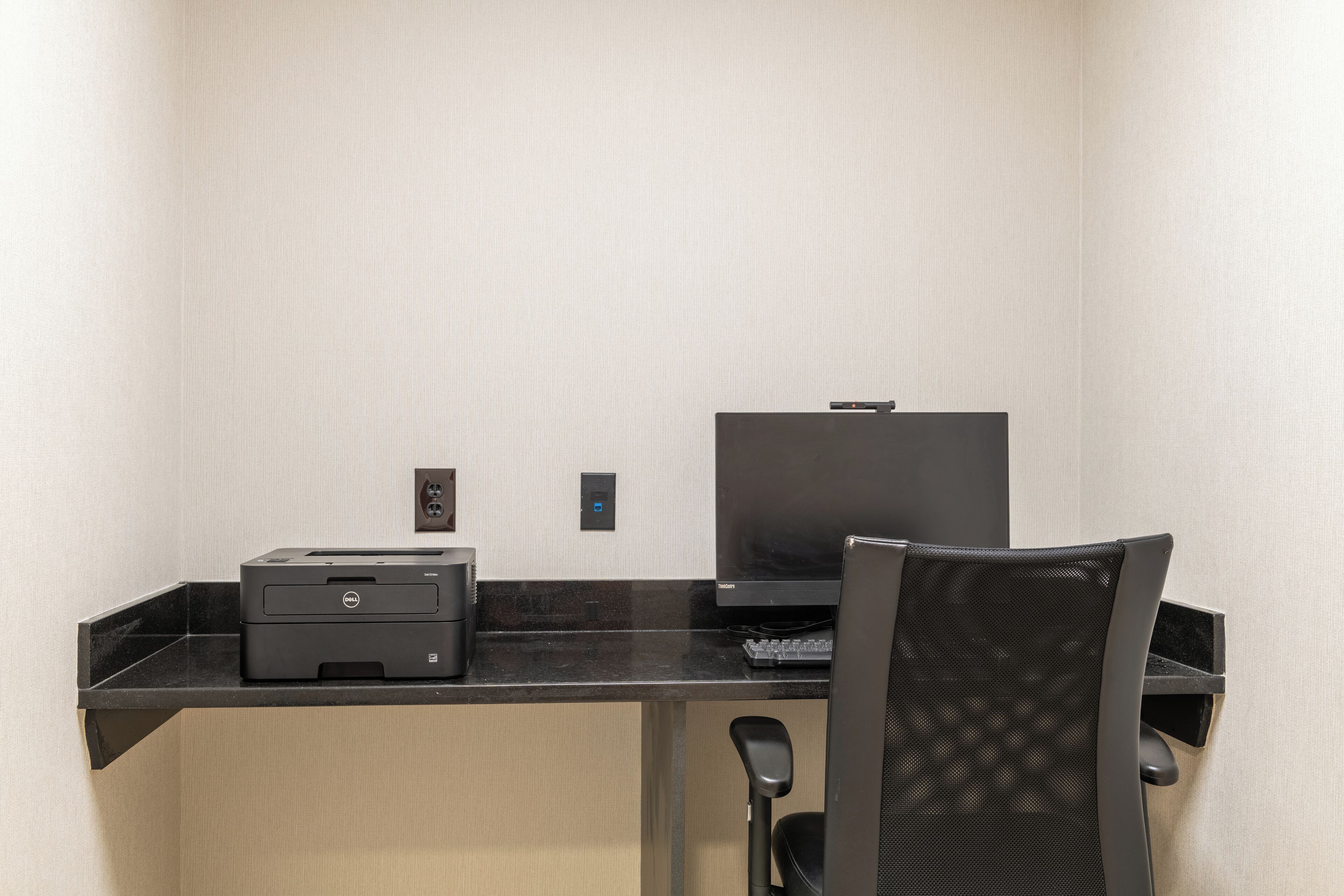 Uma mesa de escritório moderna com uma impressora, teclado e monitor.