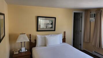 Quarto de hotel com cama, luminária, telefone, quadro na parede e janela com cortinas.