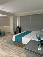 Quarto de hotel moderno com uma cama, uma escrivaninha, uma cadeira e um cesto de lixo.