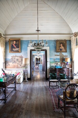 Um quarto espaçoso com piso de madeira, um lustre, uma área de jantar com cadeiras e mesa, e duas pinturas nas paredes.