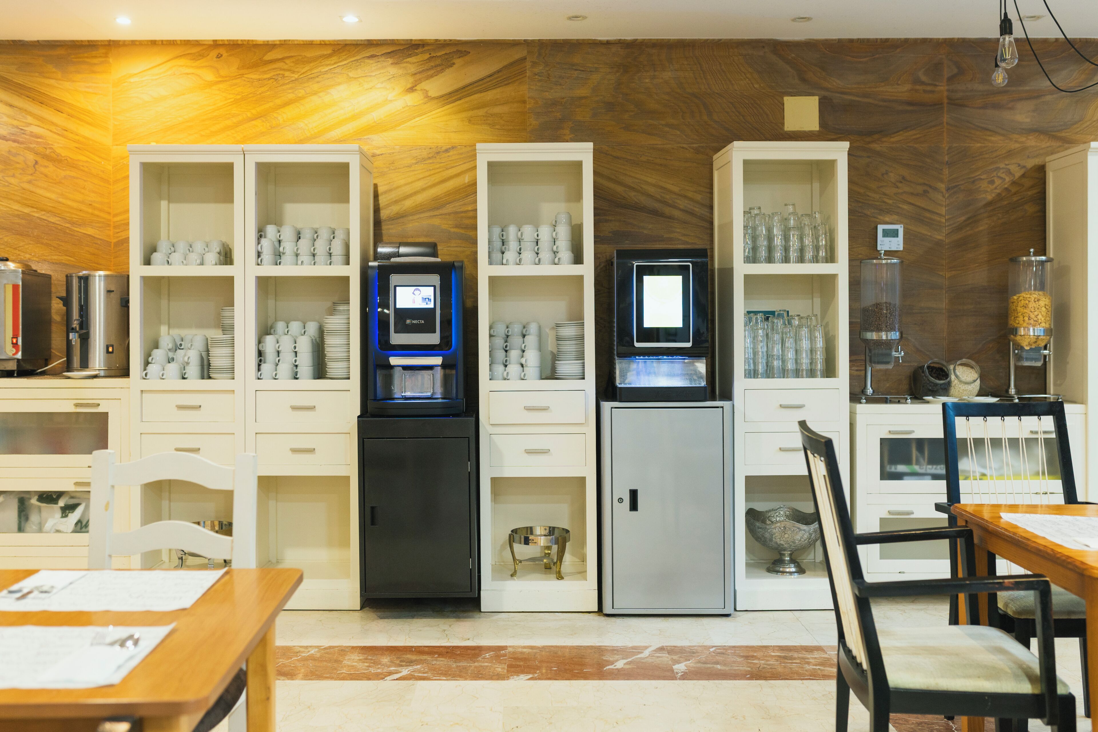 Quarto de hotel com parede de madeira, minibar, geladeira e área de refeições com cadeiras e mesa.