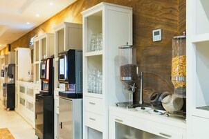 Área de recepção de hotel com totens de autoatendimento, máquina de café e peças de vidro em exposição.