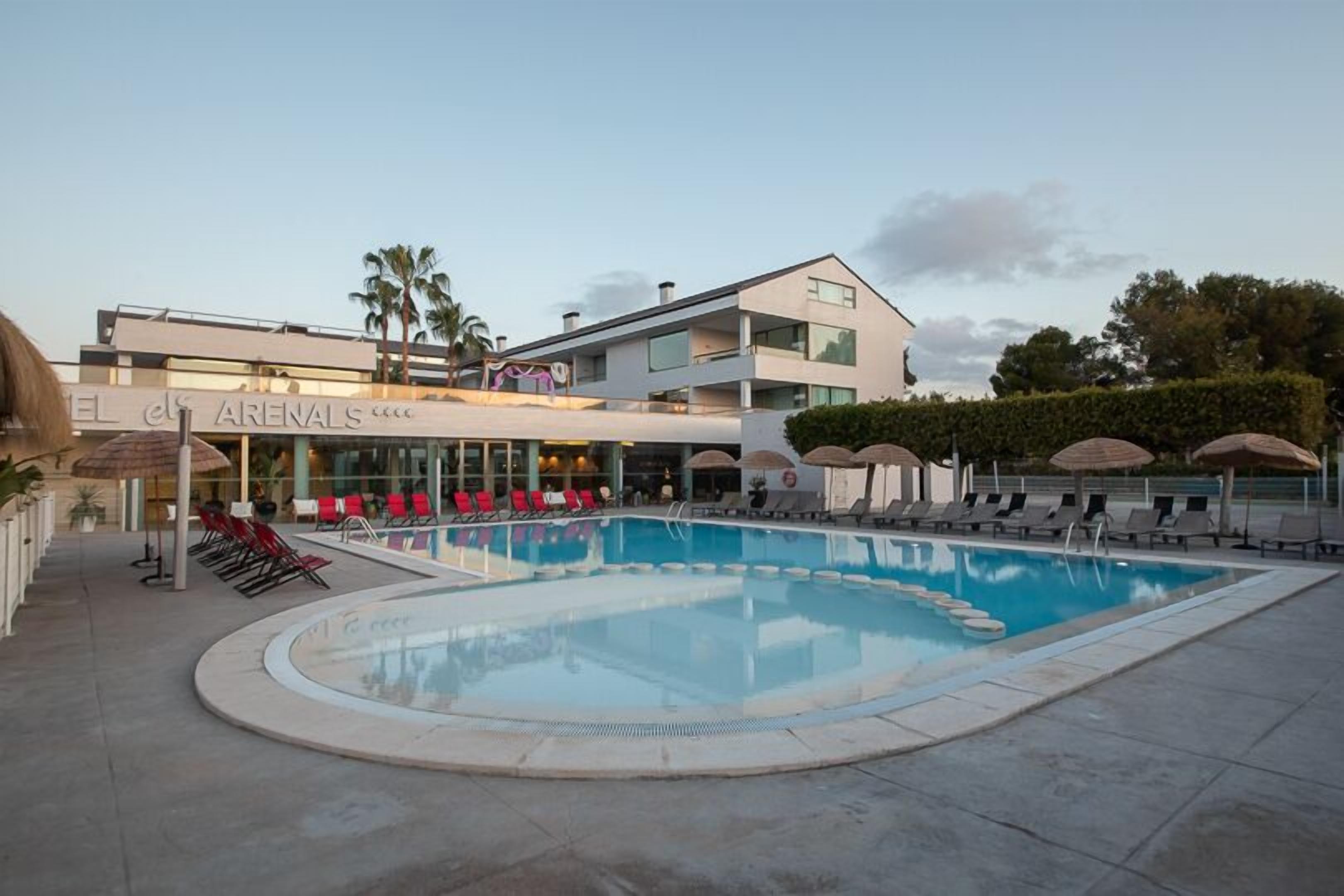 Um hotel moderno com uma grande área de piscina, espreguiçadeiras e um restaurante chamado "Hotel Arenals".