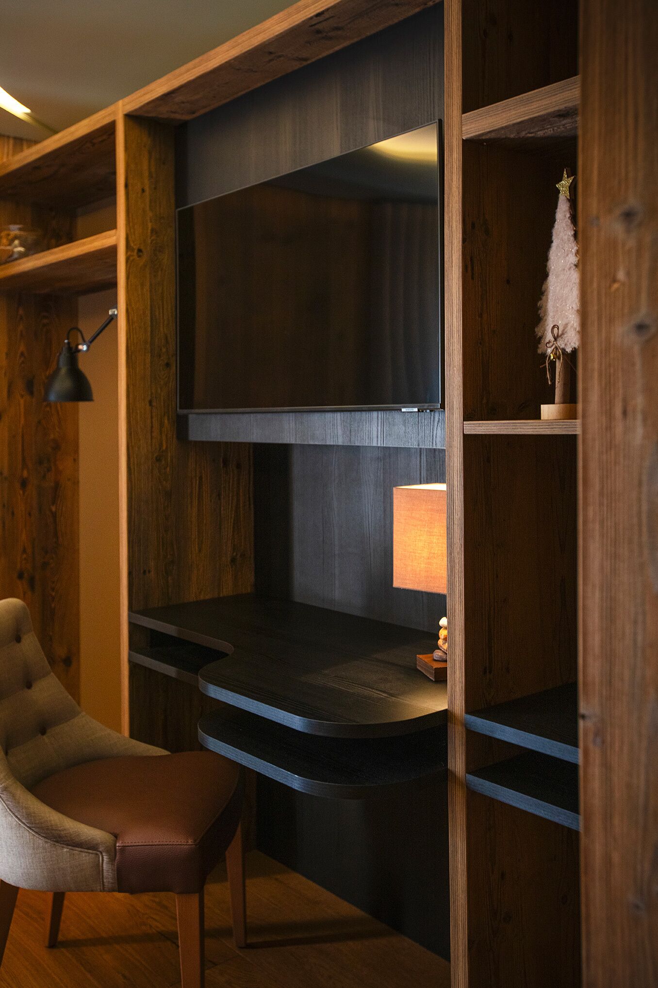 Quarto moderno com escrivaninha de madeira escura, uma poltrona confortável e uma pequena planta em uma prateleira.
