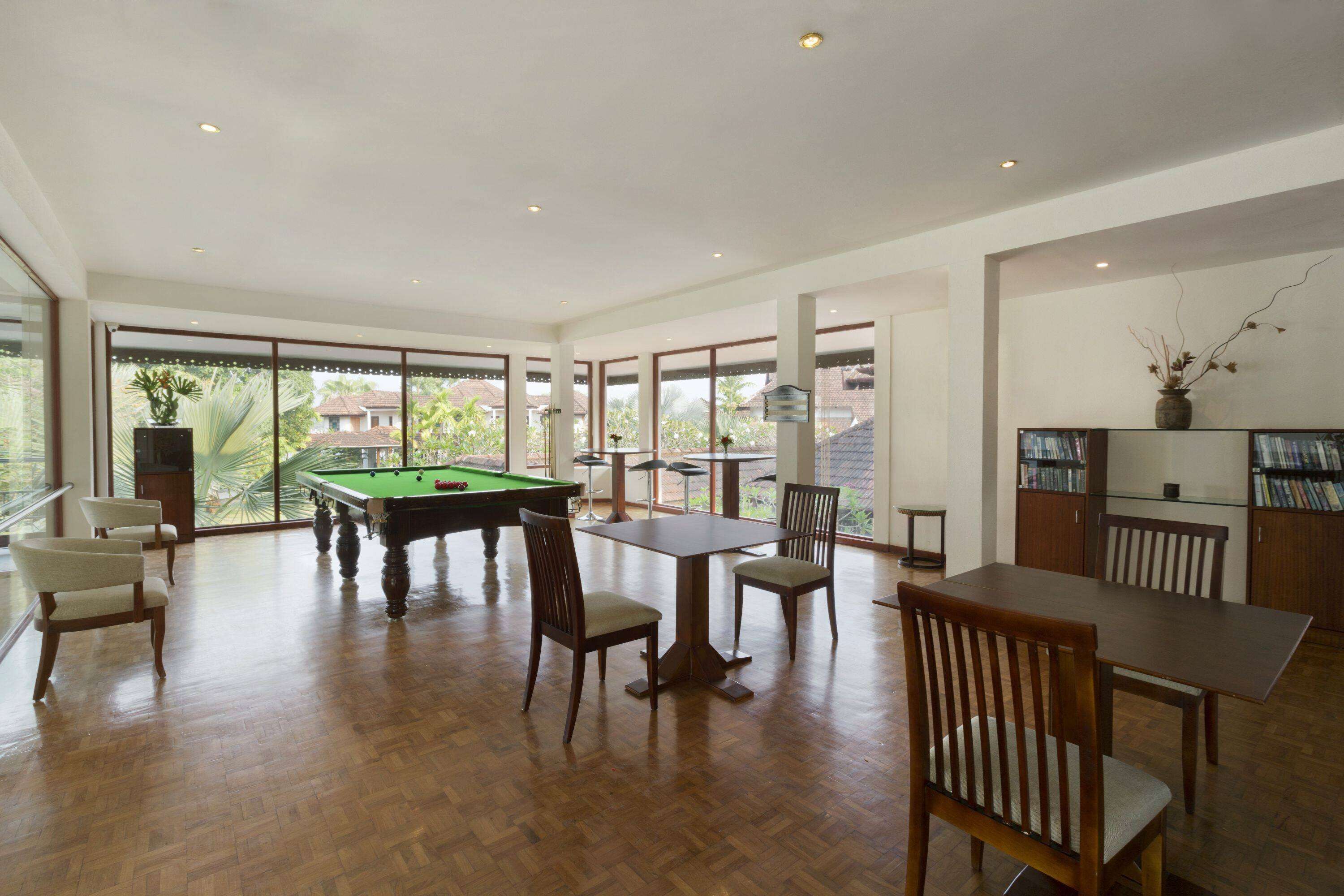 Um quarto espaçoso com mesa de bilhar, mesa de jantar e cadeiras. Janelas amplas oferecem luz natural e vista para o verde lá fora.