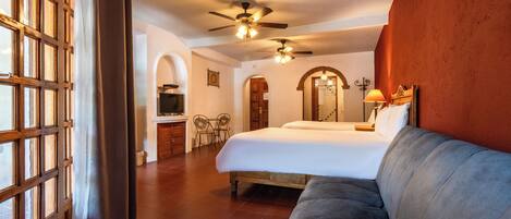 Quarto de hotel com cama grande, sofá, ventilador de teto e vista pela janela com cortinas.