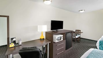 Quarto de hotel com uma cama, uma escrivaninha com abajur, micro-ondas, televisão e uma cadeira.