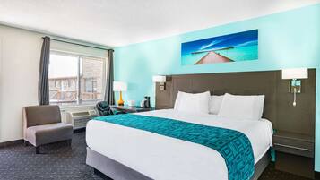 Quarto de hotel com uma cama grande, uma poltrona, uma escrivaninha com abajur e um quadro de um cais na parede.