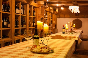Restaurante com prateleiras de madeira cheias de garrafas, mesa com toalha quadriculada, velas e taças de vinho.