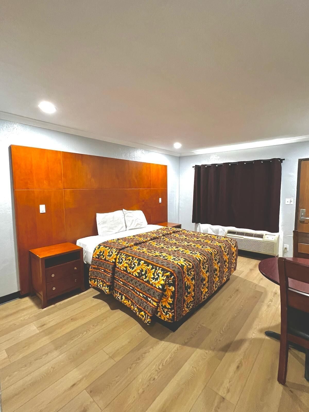 Quarto com cabeceira de madeira, cama com colcha estampada, mesa de cabeceira e uma cadeira.