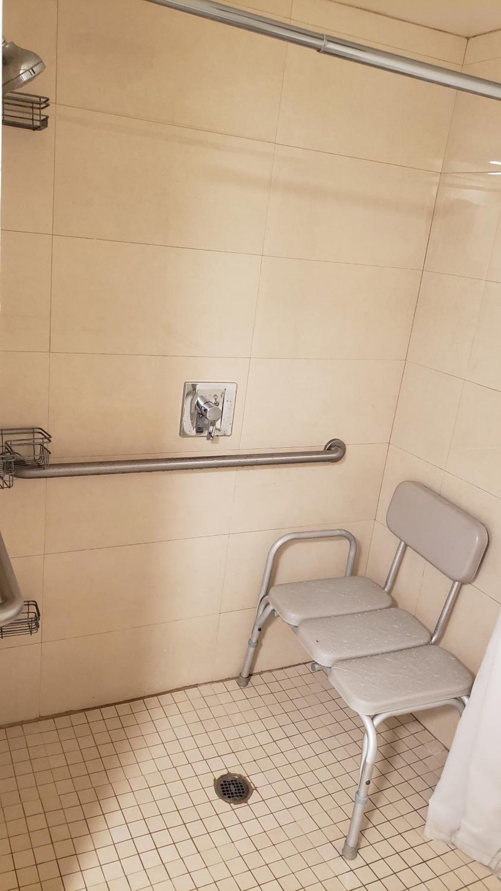 Um box de chuveiro pequeno, revestido com azulejos, com barra de apoio, chuveiro e assento.