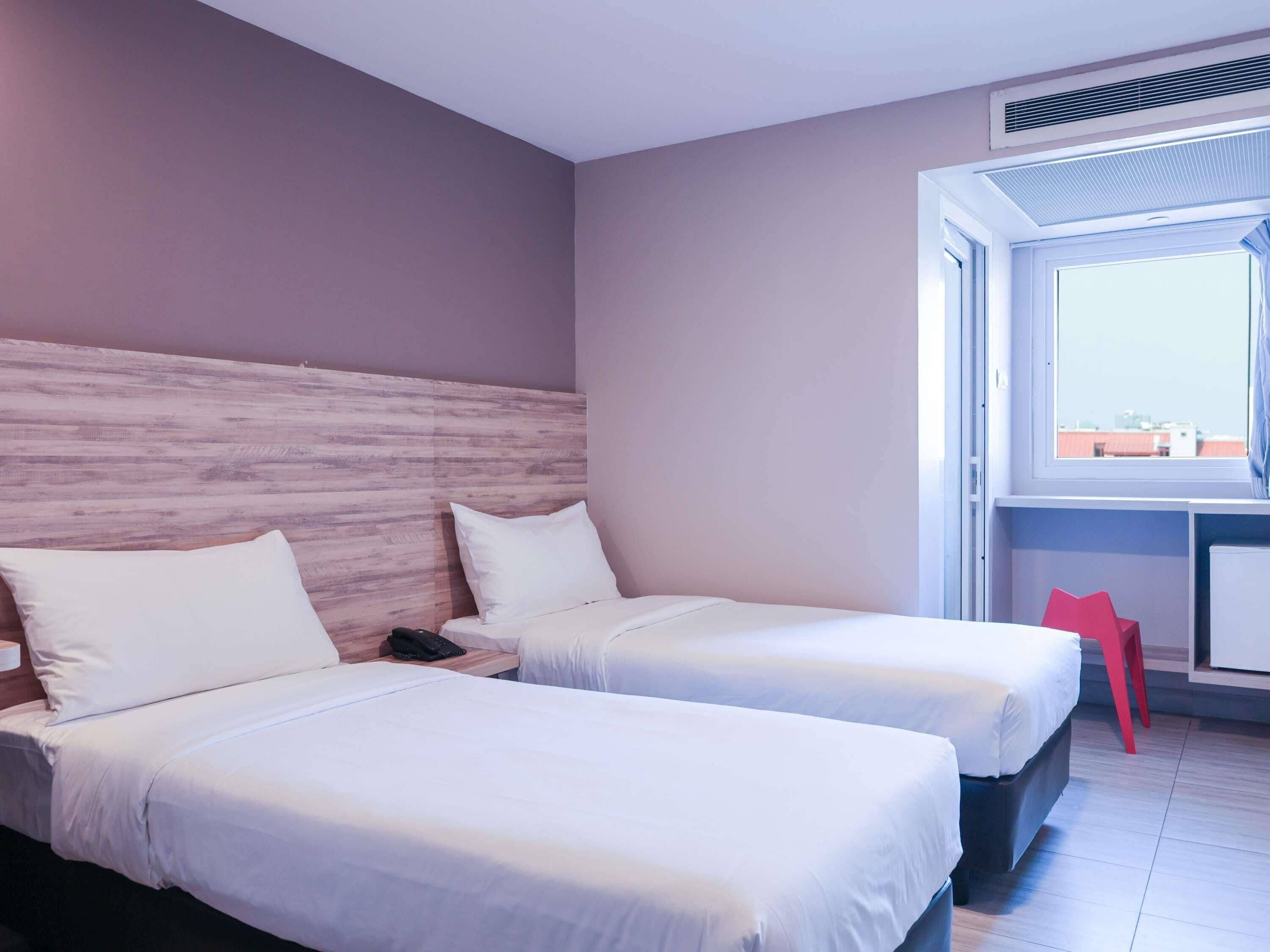 Quarto de hotel com duas camas, cabeceira de madeira, escrivaninha com cadeira e janela com vista.