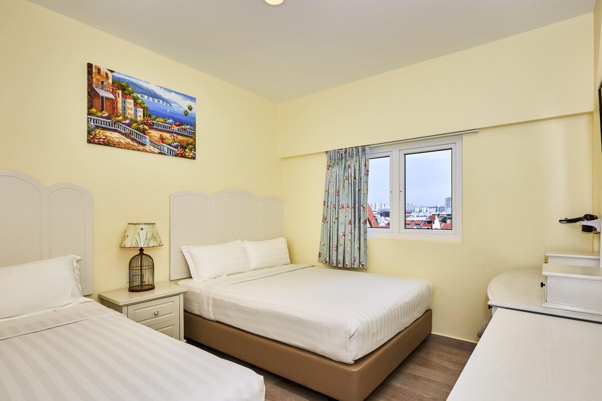 Quarto de hotel com duas camas, uma janela com cortinas, um quadro na parede e um abajur na mesa de cabeceira.