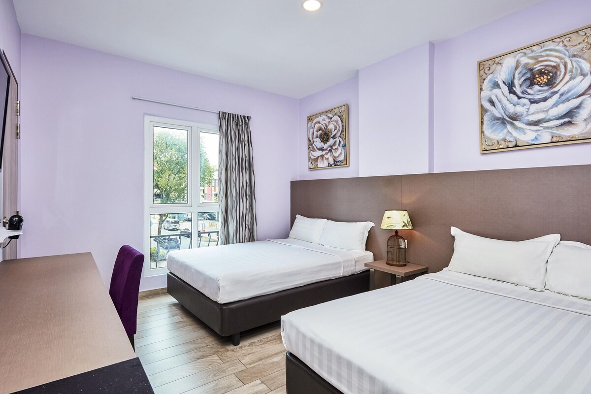Quarto de hotel com duas camas, uma escrivaninha, uma cadeira e uma janela com cortinas.