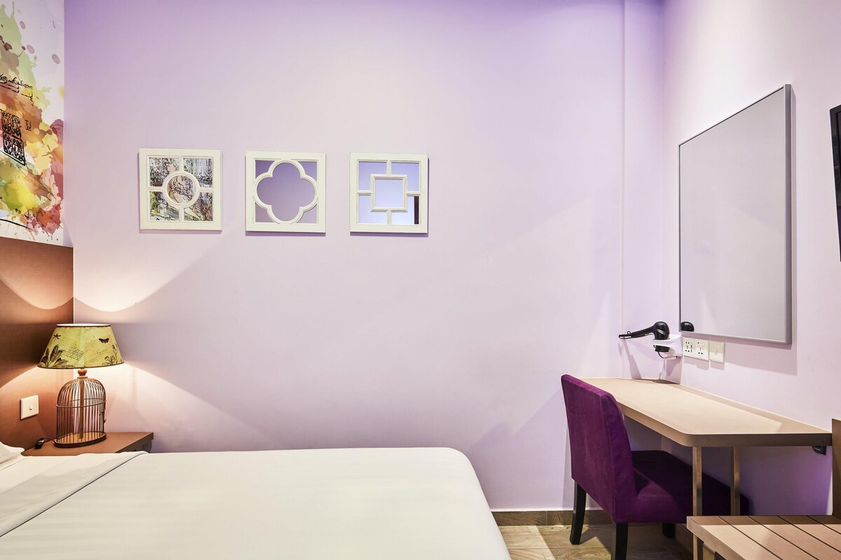 Quarto de hotel com cama, escrivaninha, cadeira, luminária e obras de arte nas paredes.